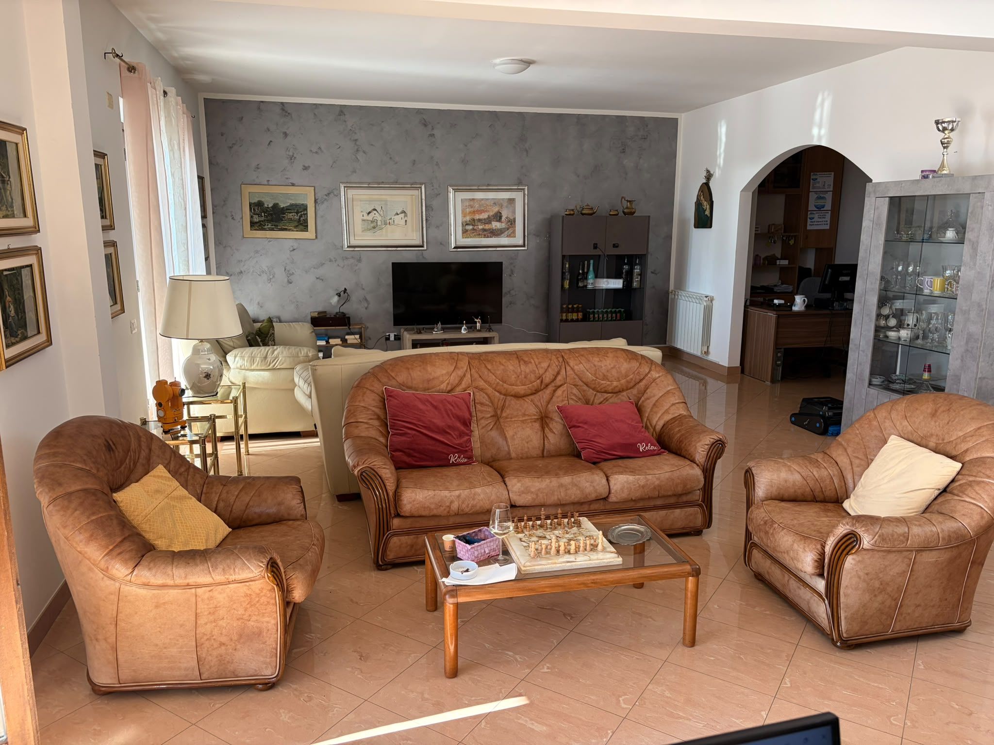 Uma sala de estar com um sofá de couro marrom, uma mesa de centro com peças de xadrez e uma televisão.