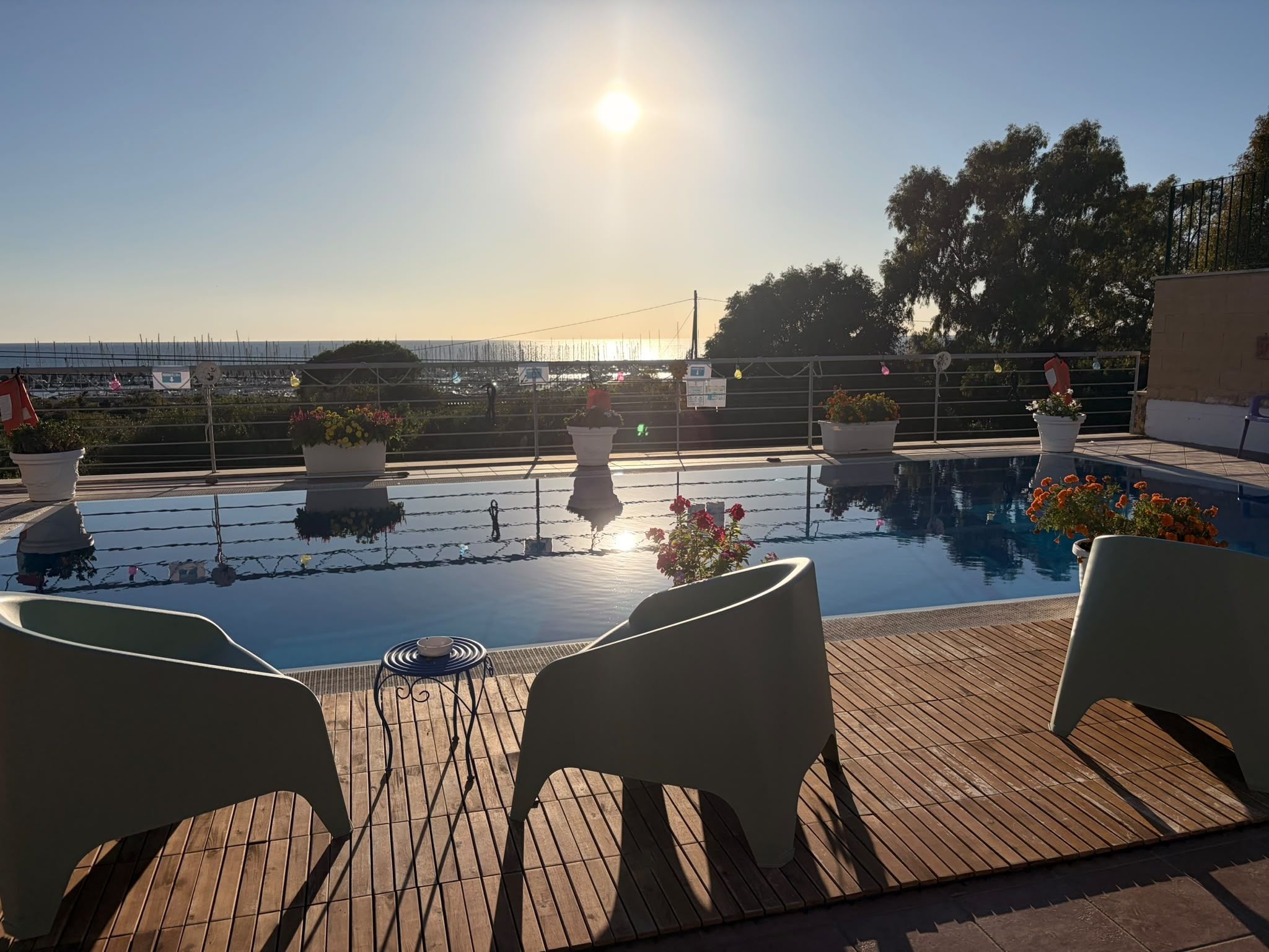 Piscina com vista para o mar, rodeada por plantas em vasos e espreguiçadeiras.