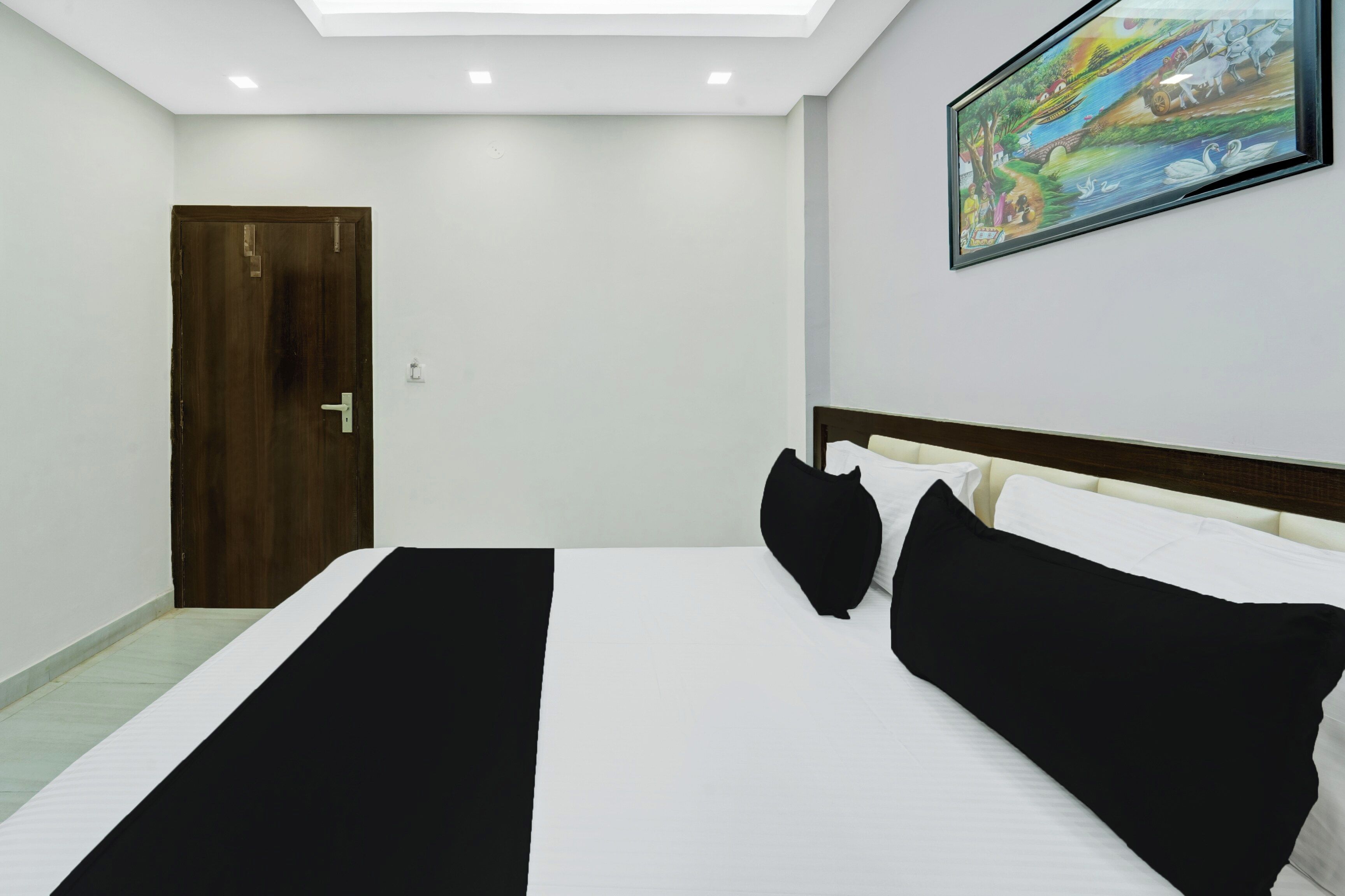 Quarto com cama, porta, quadro na parede e luminária no teto.