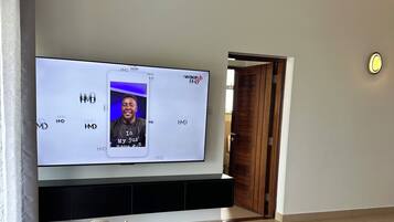 Sala de estar com televisão de tela plana na parede, ventilador de teto, sofá e tapete estampado.