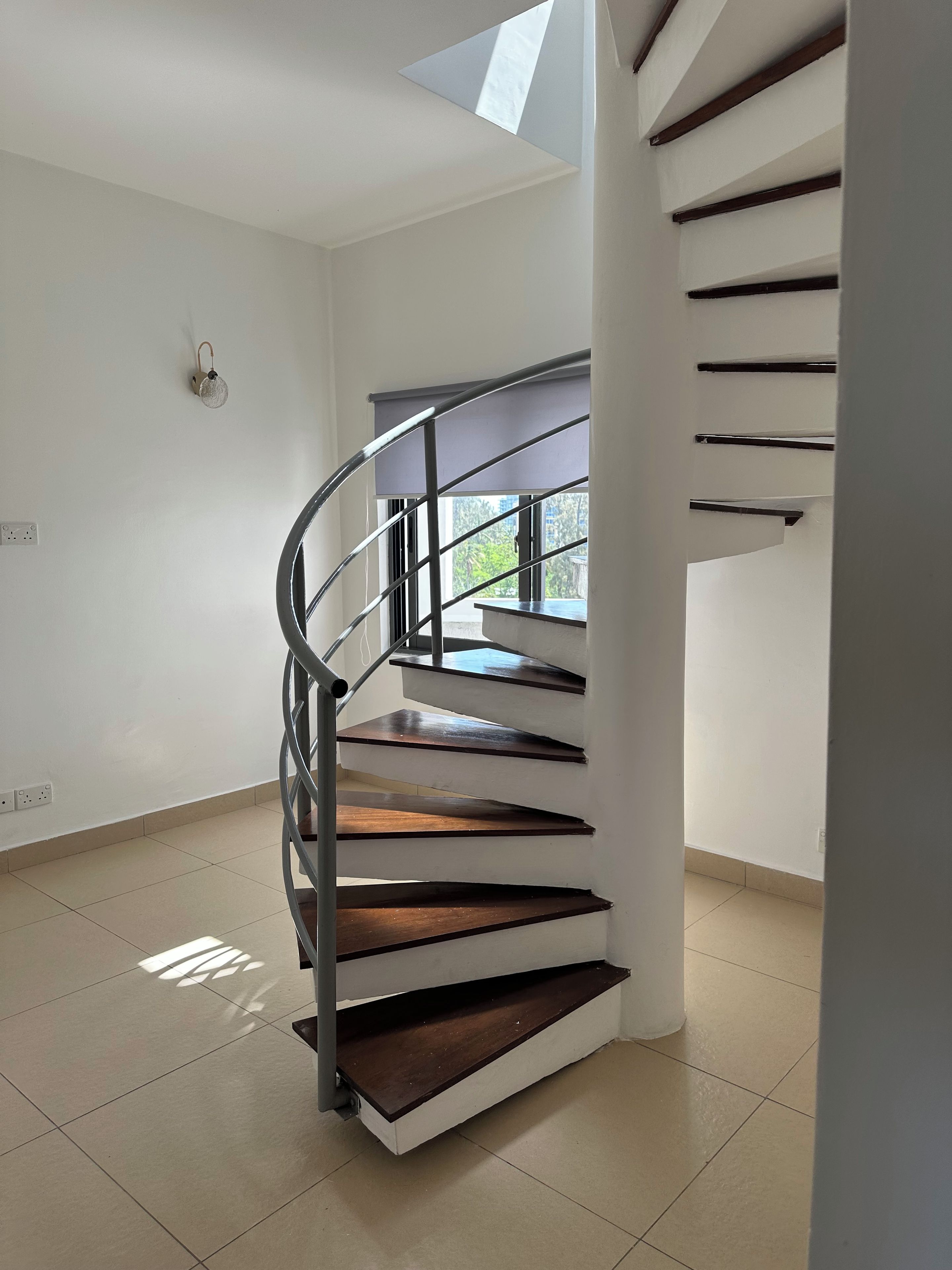Uma escadaria em espiral com degraus de madeira e corrimãos de metal, que dá acesso a um andar superior.