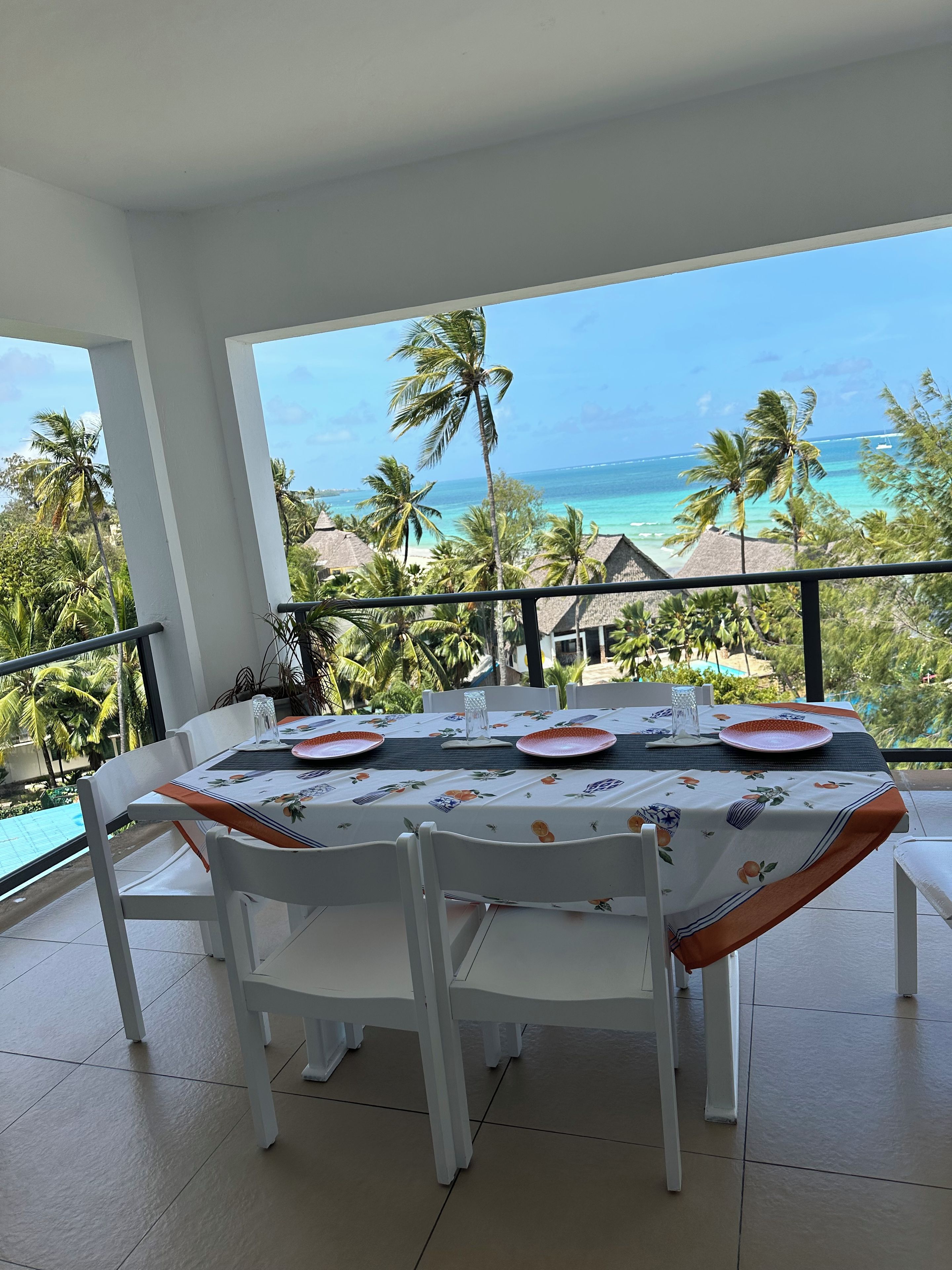Mesa de jantar posta para dois, vista para o oceano e palmeiras.