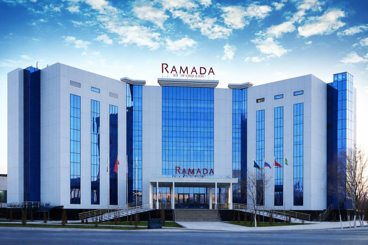 Um edifício moderno com o nome 'RAMADA' em destaque na fachada.