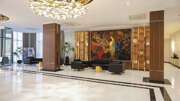 Um saguão de hotel com um grande mural, área de estar e um lustre moderno.
