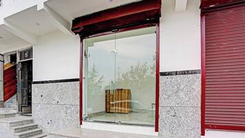 Entrada de prédio com porta de vidro, degraus de acesso e toldo vermelho.