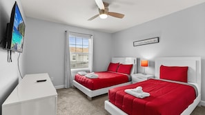 Quarto de hotel com duas camas, televisão, ventoinha no teto e janela com persianas.