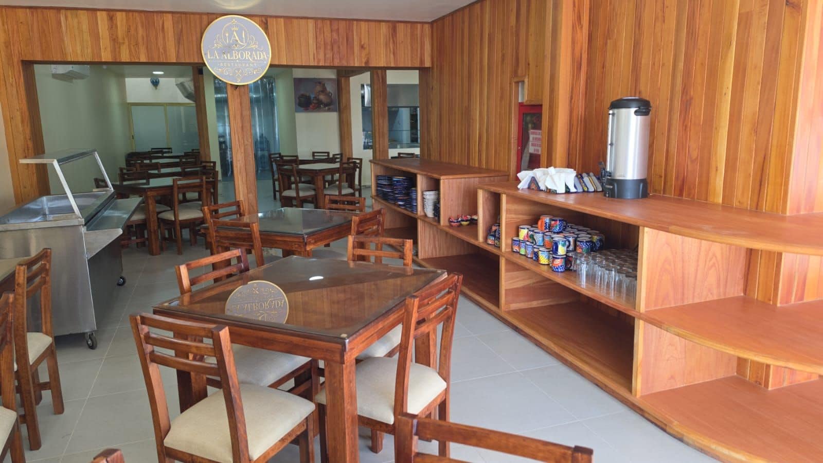 Interior de restaurante com móveis de madeira, balcão com bebidas e placa indicando ser um restaurante.