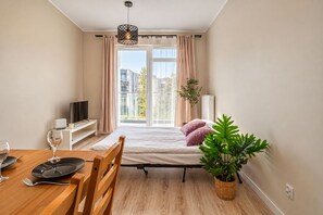 Quarto moderno com cama, televisão, mesa de jantar com cadeiras e um vaso de planta.
