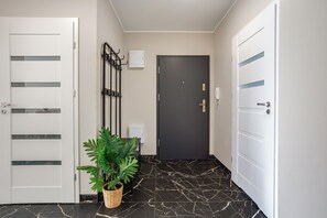 Um corredor com uma porta escura, uma porta branca com ripas horizontais e uma planta em vaso.