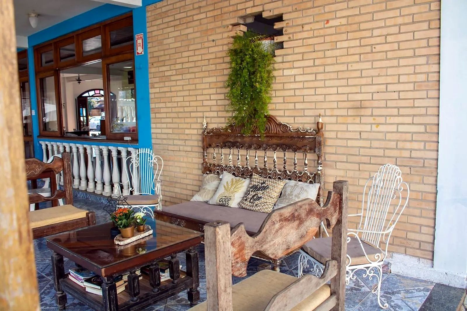 Uma área de estar acolhedora ao ar livre, com um banco de madeira, uma mesa com livros e flores, e uma cabeceira decorativa.