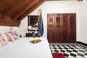 Quarto com cama, guarda-roupa de madeira, espelho e uma mesinha com abajur.