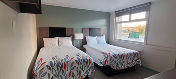 Quarto de hotel com duas camas, janela com vista para o exterior e televisão de tela plana fixada na parede.