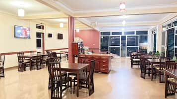 Uma sala de jantar ampla com várias mesas e cadeiras, uma ilha central com pia e bancada, e grandes janelas que proporcionam iluminação natural.