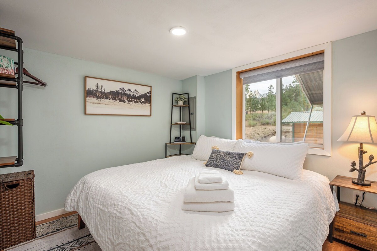 Quarto com uma cama grande, uma mesa de cabeceira com abajur, um quadro na parede e uma janela com vista para o exterior.