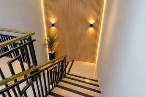 Uma escadaria com piso em faixas preta e branca, um vaso de planta e luminárias fixadas na parede.