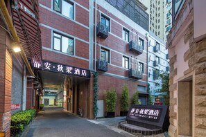 Entrada de hotel com placa em chinês e inglês, fachada de tijolos e rua estreita.