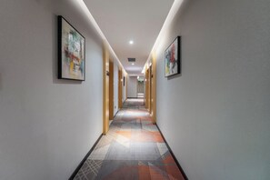 Corredor de hotel com quadros nas paredes, um tapete estampado e uma luminária no teto.