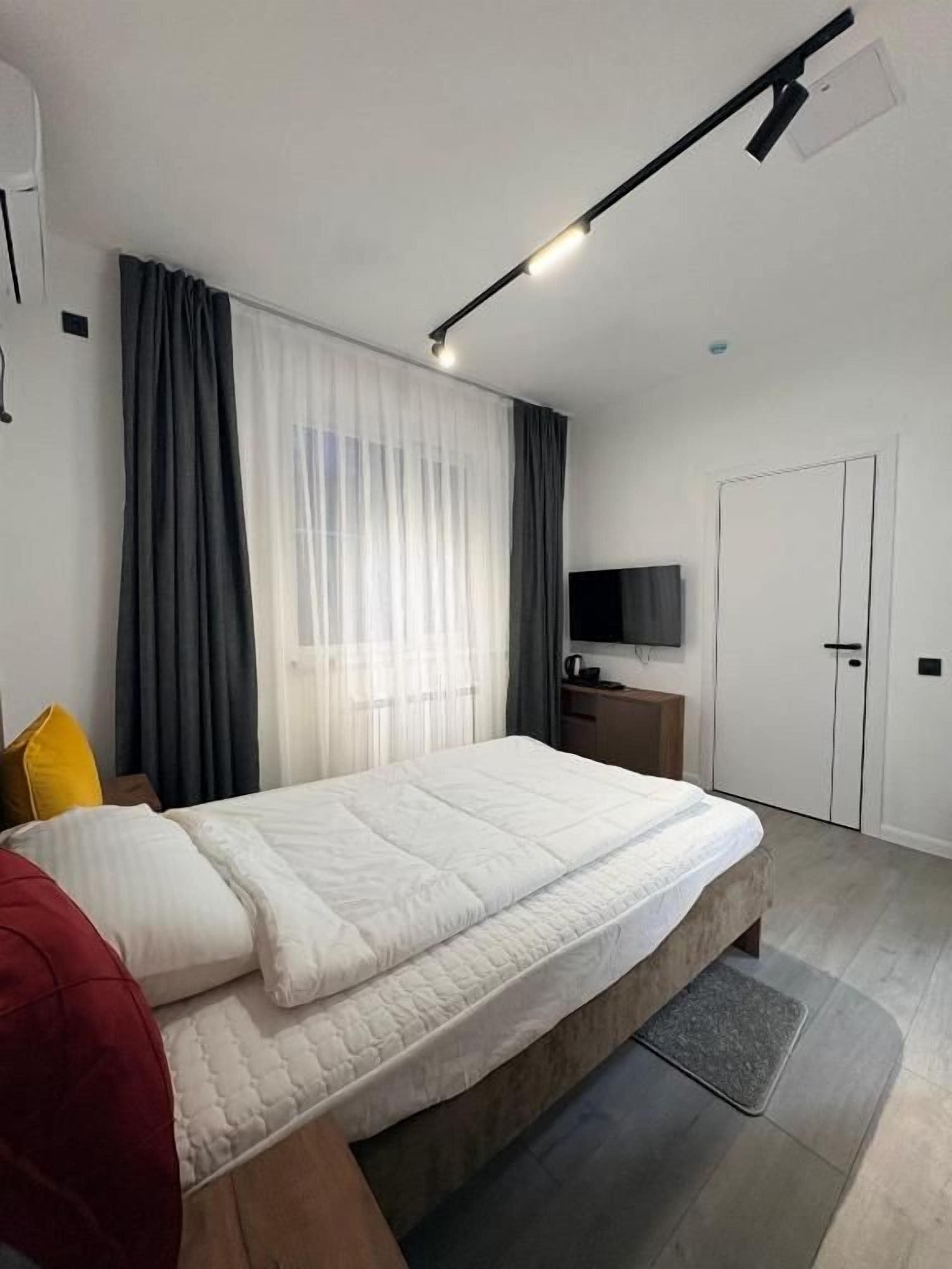 Quarto moderno com cama, cortinas, televisão e guarda-roupa.
