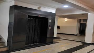 Corredor com elevador preto, escada e porta que dá para outro cômodo.