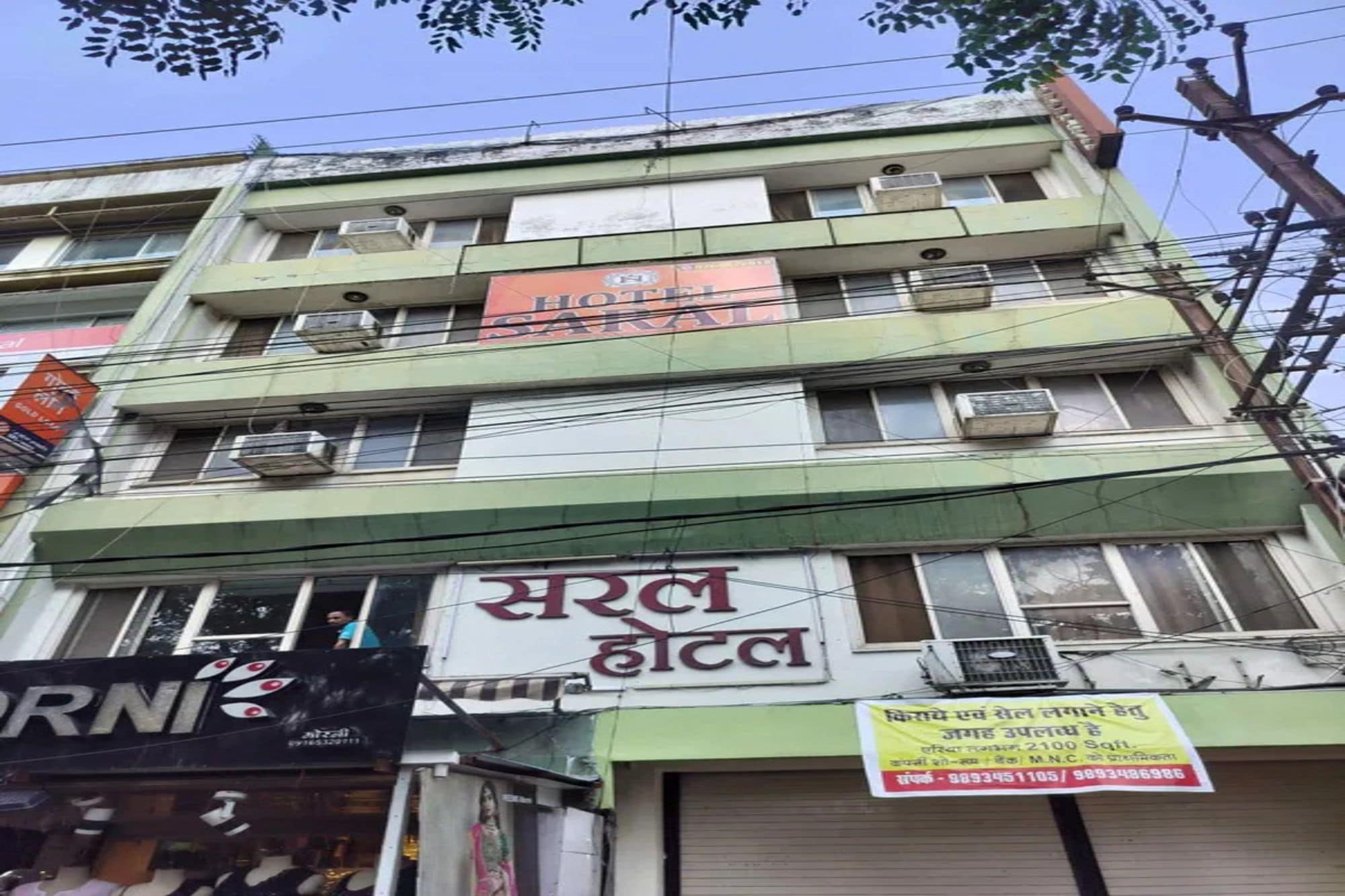 Um edifício com vários andares, placa de hotel, aparelhos de ar condicionado e fachada comercial com sinalização em idioma local.