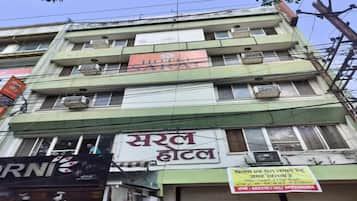 Um edifício com vários andares, placa de hotel, aparelhos de ar condicionado e fachada comercial com sinalização em idioma local.