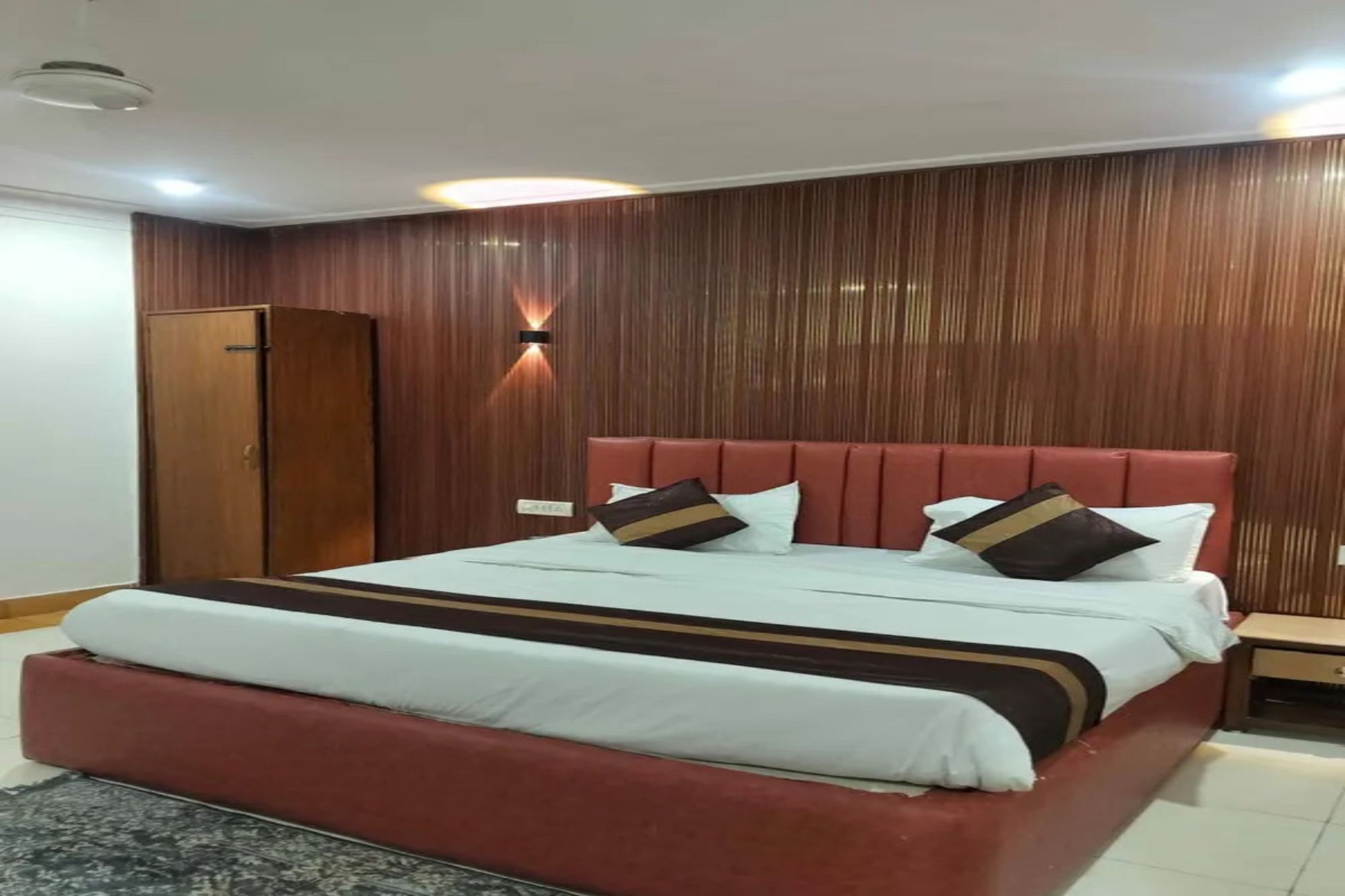 Quarto com cama grande, guarda-roupa e luminária na parede.