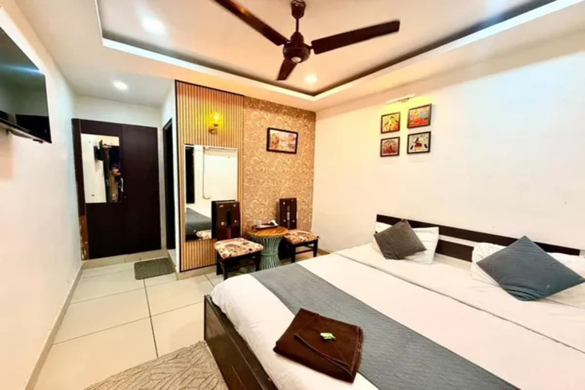 Quarto de hotel com cama, escrivaninha, cadeira, ventilador de teto e parede com quadros.