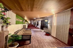 Um corredor com teto de madeira, plantas em vasos, um banco e portas à direita.