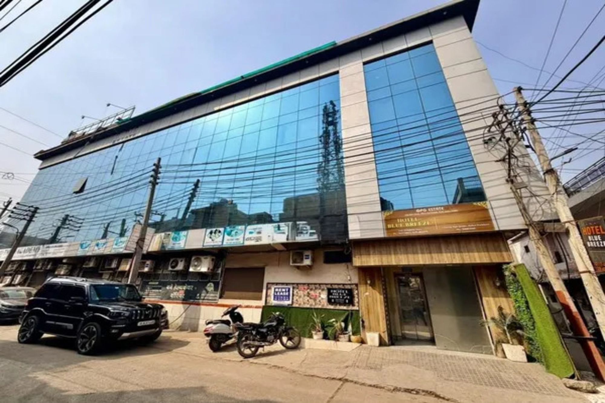 Um edifício moderno com fachada de vidro refletiva, placa indicando um hotel, e um carro e uma motocicleta estacionados na frente.