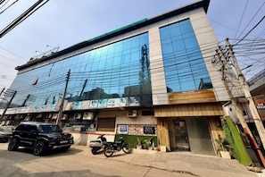 Um edifício moderno com fachada de vidro refletiva, placa indicando um hotel, e um carro e uma motocicleta estacionados na frente.
