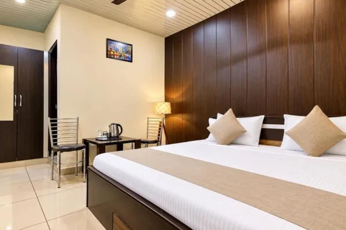Quarto de hotel com uma cama grande, uma escrivaninha, duas cadeiras, uma cafeteira e um quadro na parede.