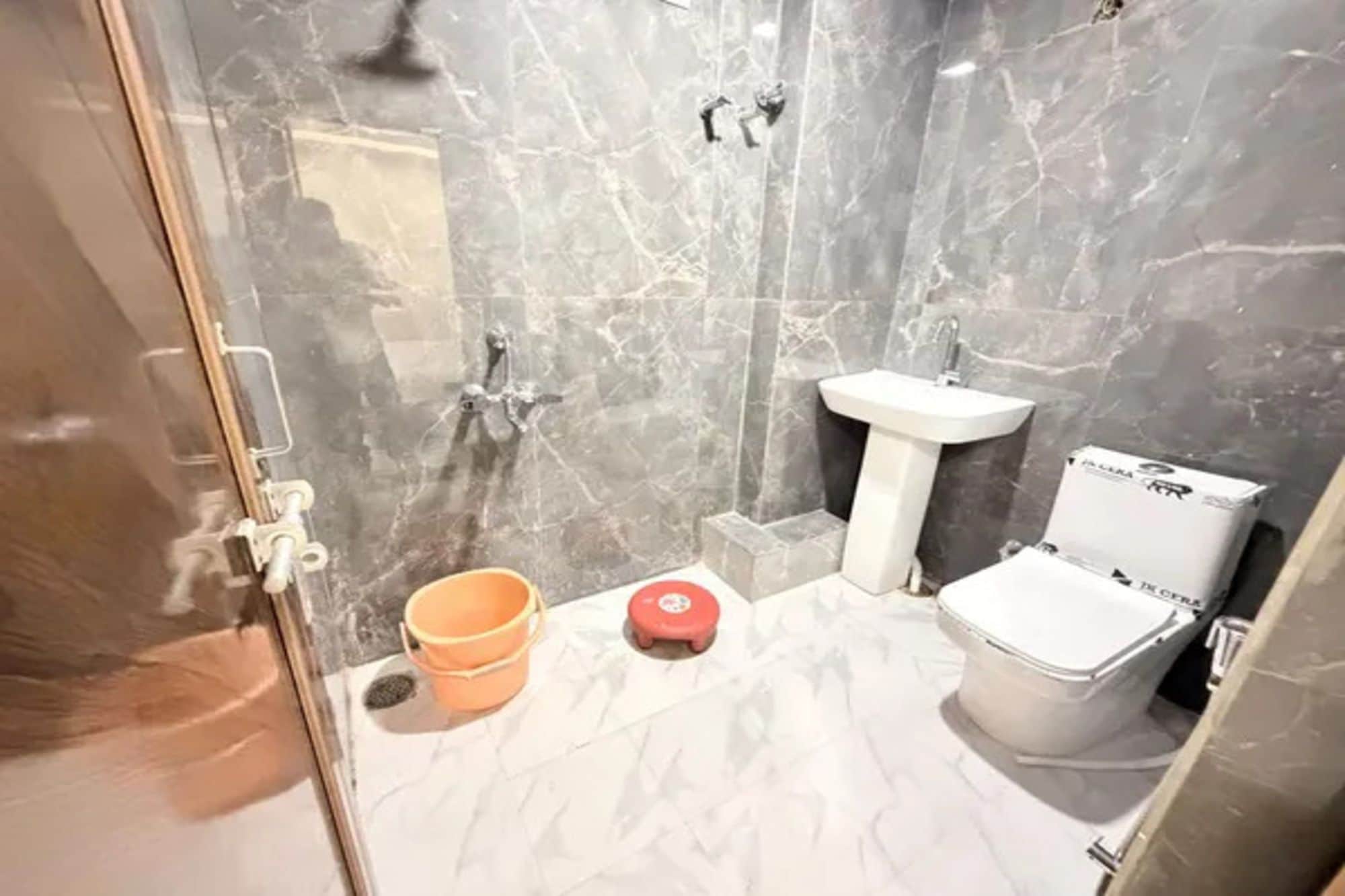 Casa de banho com soalho de mármore, lavatório branco, sanita e zona de duche.