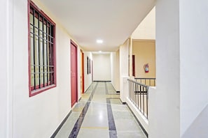 Um corredor com piso de azulejos, portas e um extintor de incêndio na parede.