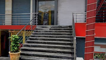 Um conjunto de degraus de mármore preto que levam à entrada de um edifício, com uma porta de vidro, um toldo vermelho e um guarda-corpo de metal.