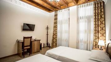 Quarto de hotel com duas camas, uma mesa de trabalho com cadeira, televisão e um cabideiro.