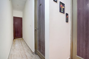 Corredor com porta de madeira identificada com o número '103' e parede branca com duas imagens emolduradas.