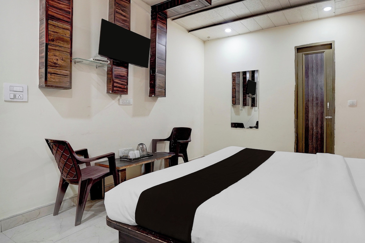 Quarto de hotel com cama, escrivaninha com cadeira, televisão na parede e uma porta.