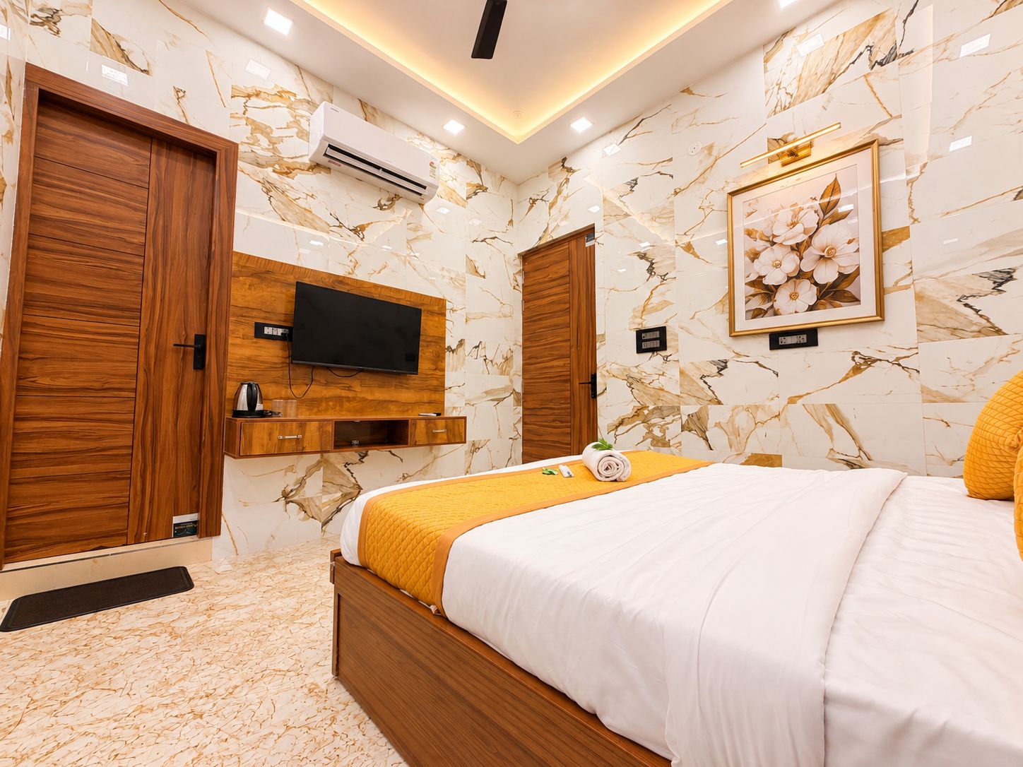 Quarto de hotel com cama de madeira, paredes com padrão marmorizado, televisão montada e quadro floral emoldurado.