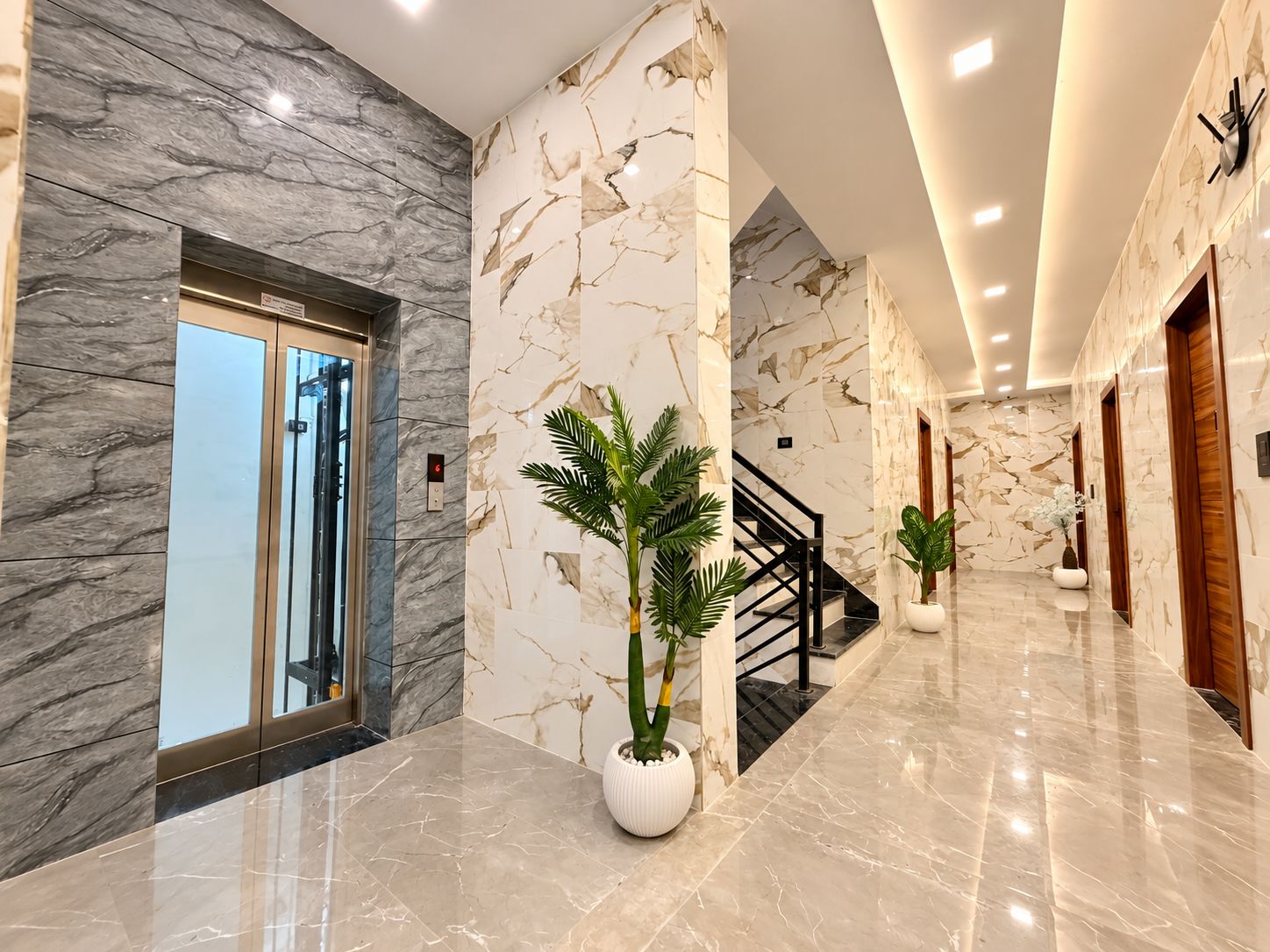Um hall de hotel moderno com paredes de mármore, um elevador de vidro, uma escadaria e plantas em vasos.