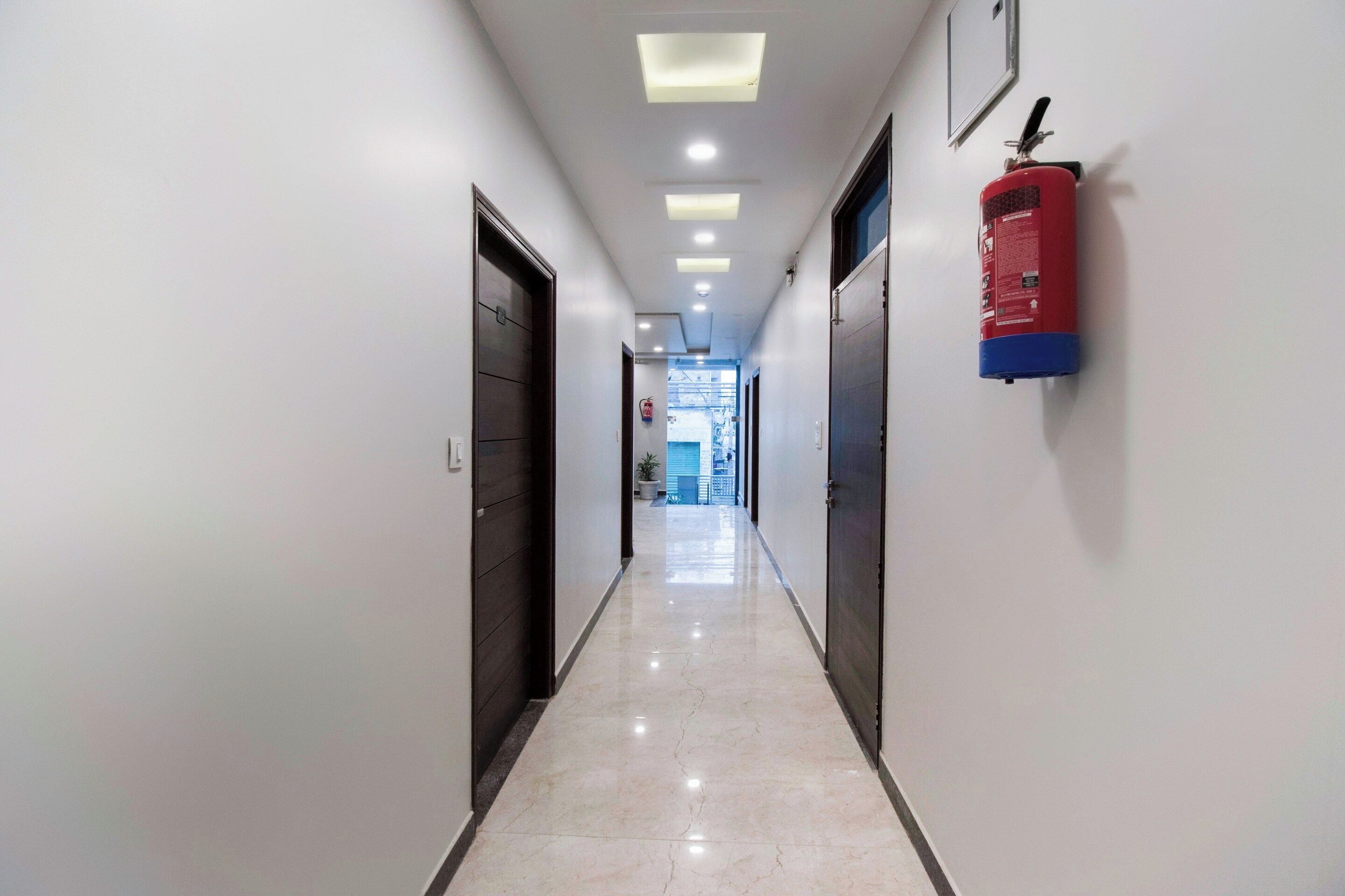Um corredor com portas em ambos os lados, um extintor fixado na parede e teto com iluminação embutida.