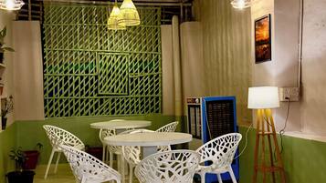 Quarto com divisória de treliça verde, cadeiras brancas, mesa redonda e abajur.