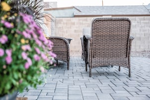 Móveis de jardim em vime com mesa e cadeiras, dispostos numa área externa pavimentada com um muro de tijolos ao fundo.