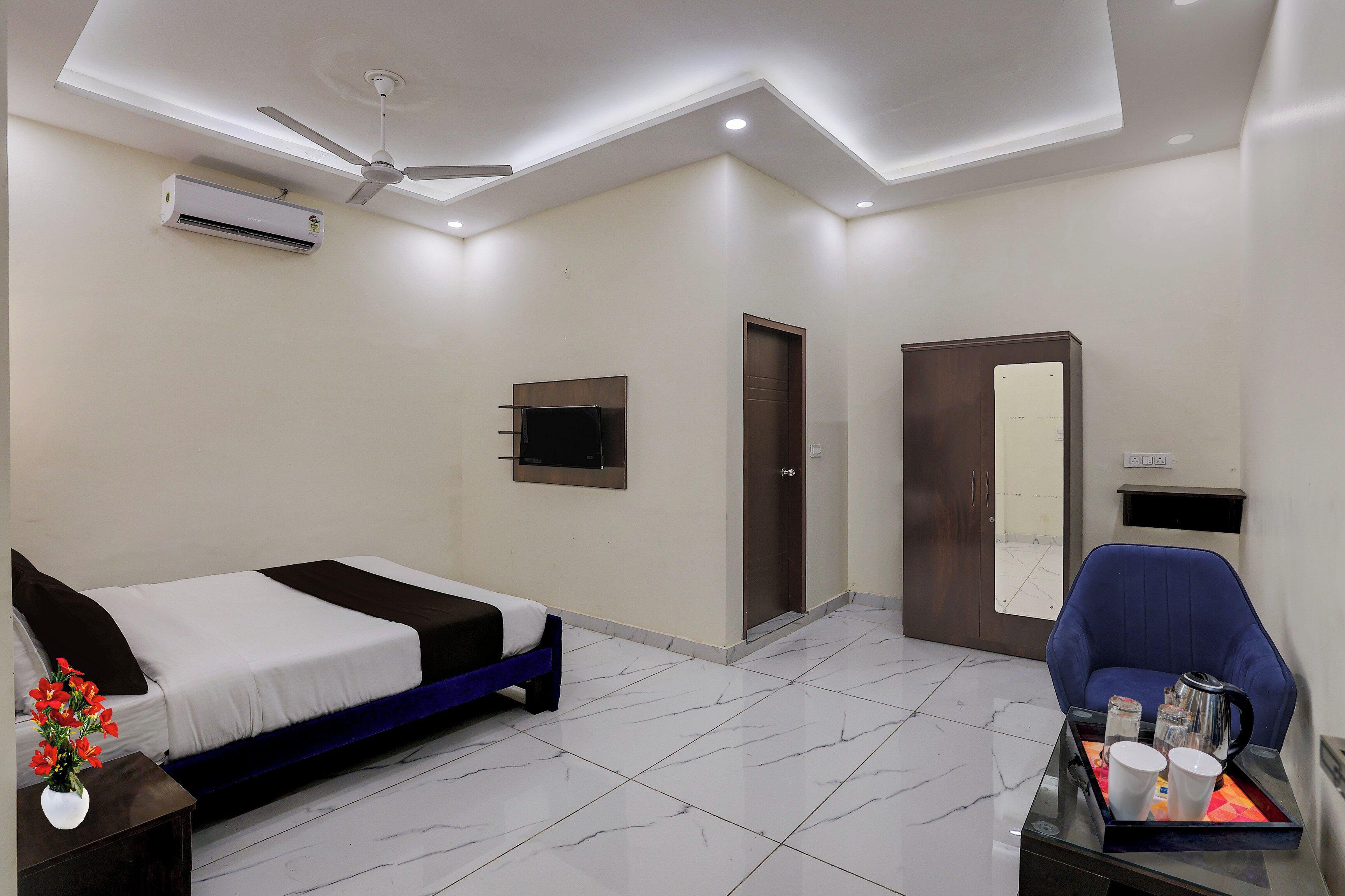 Quarto de hotel com uma cama, uma escrivaninha com bandeja de copos, uma cadeira, um guarda-roupa, uma porta e um aparelho de ar condicionado.