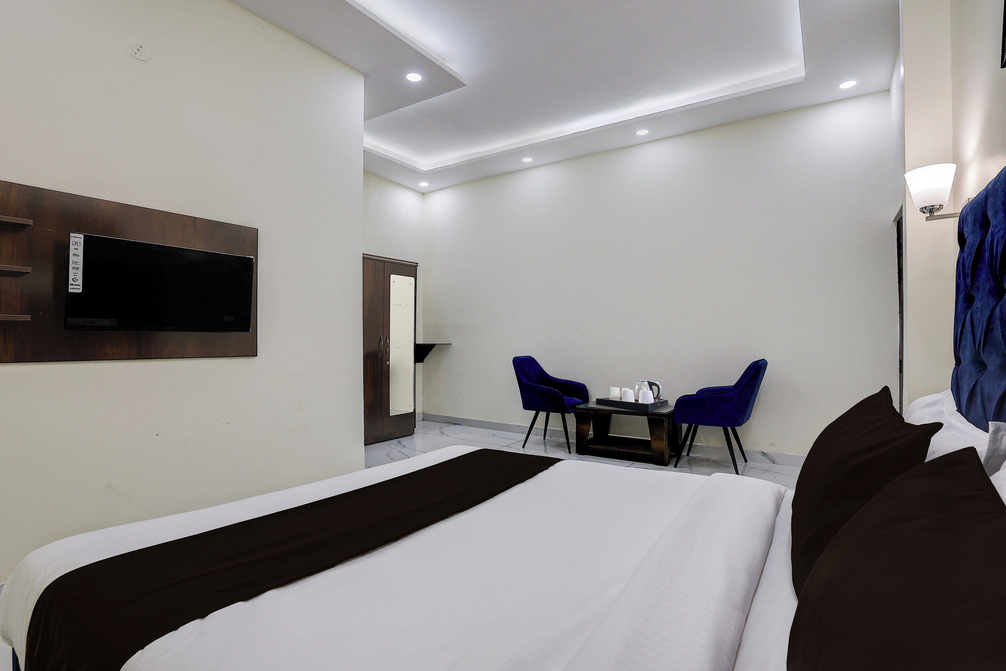 Quarto de hotel com cama, escrivaninha e duas cadeiras, televisão na parede e espelho.