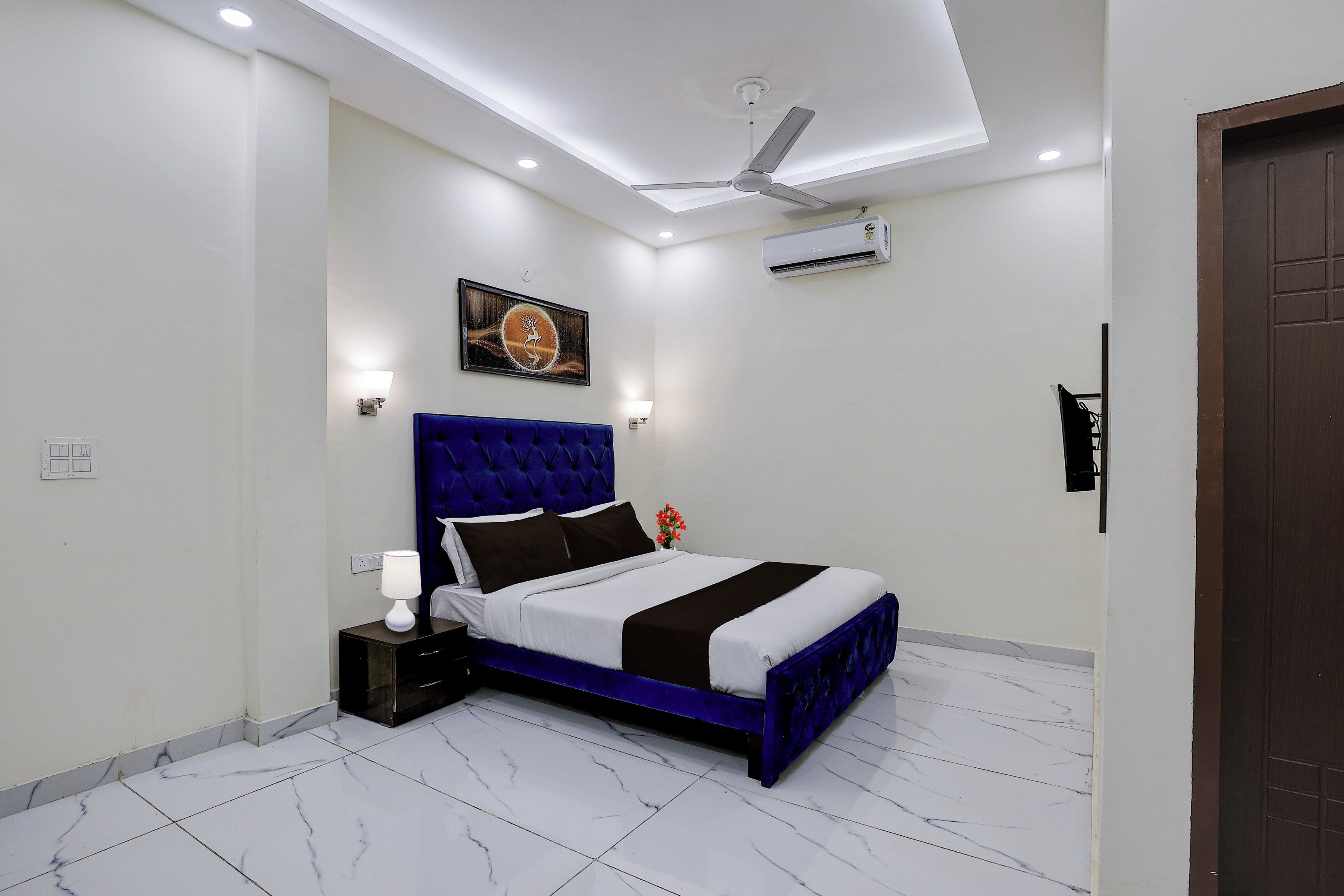 Quarto com cama, mesa de cabeceira, luminária na parede, ventoinha no teto e ar condicionado.