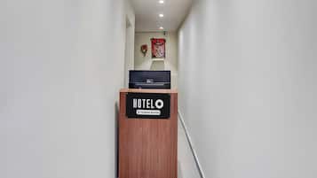 Uma área de recepção de hotel com um balcão de madeira com a etiqueta 'HOTELO' e uma placa indicando 'Serviço para Empresas'.
