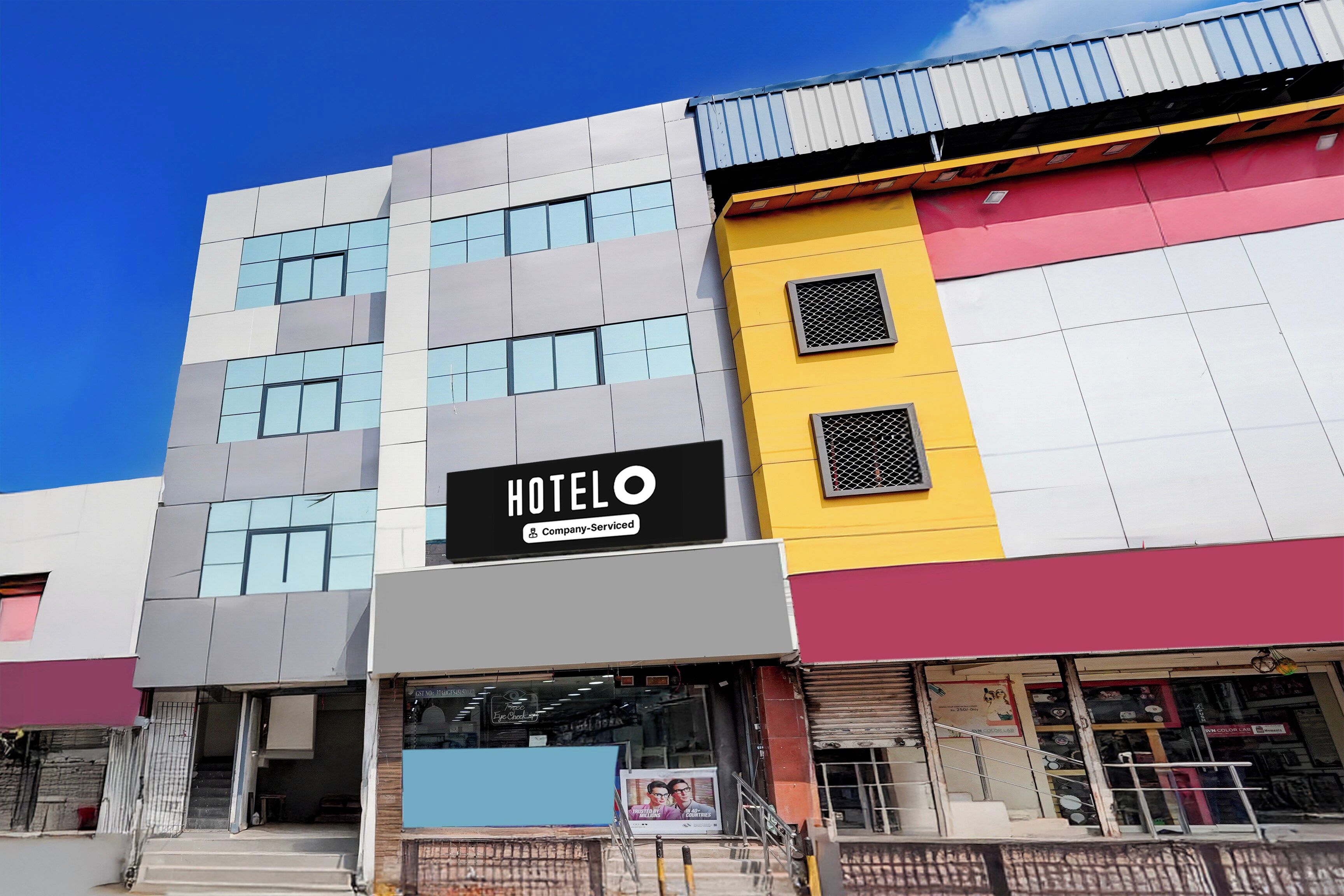 Um hotel com vários andares, um letreiro chamativo 'HOTELO', janelas amplas e uma combinação de cores neutras e vibrantes na fachada.