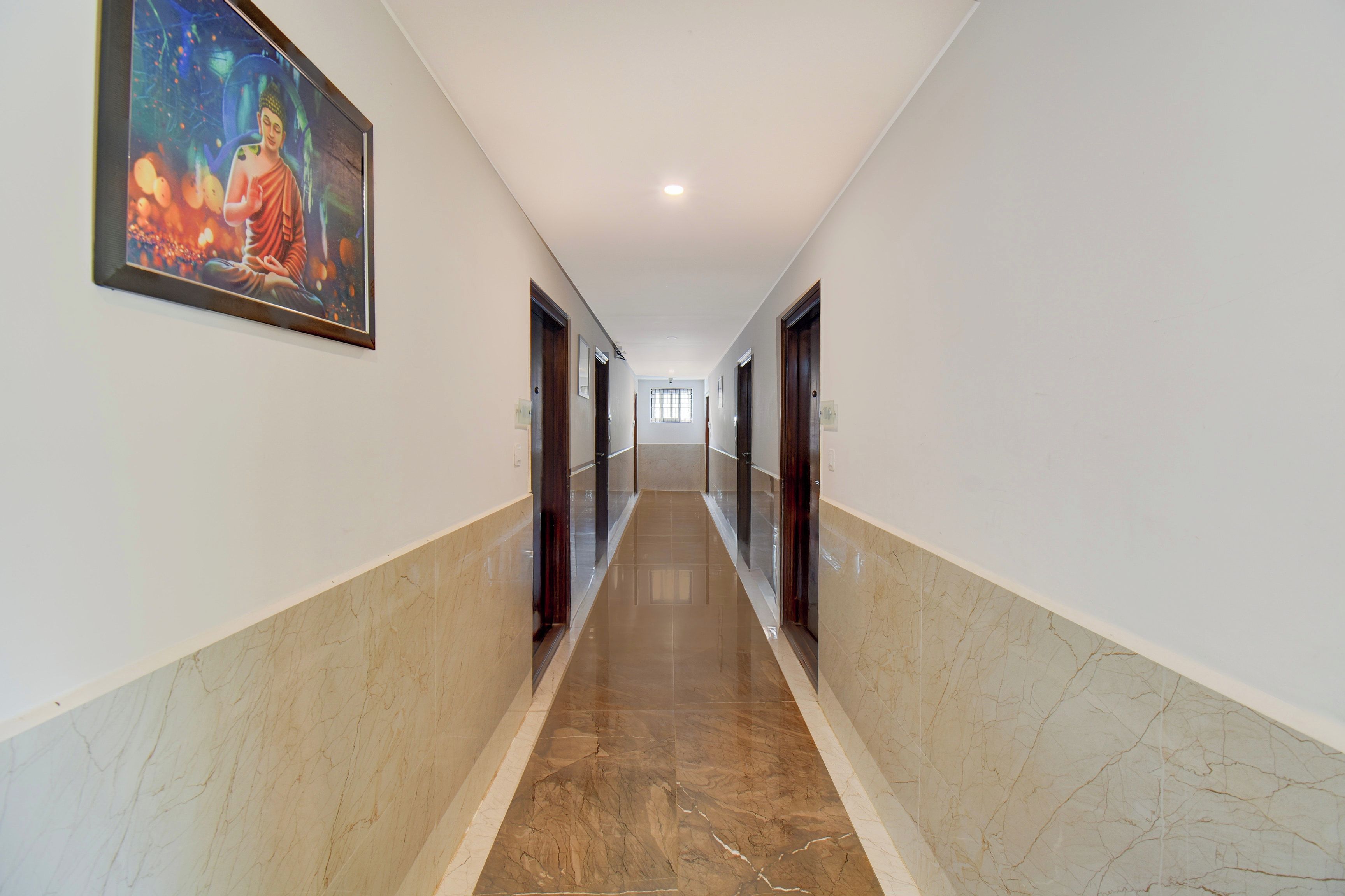 Corredor com piso de mármore, um quadro na parede esquerda e portas em ambos os lados.