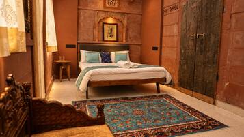 Quarto tradicional com uma cama, guarda-roupa de madeira, mesa pequena e um tapete decorativo.