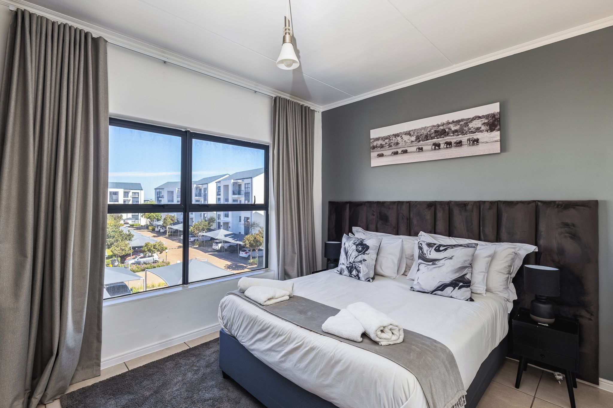 Quarto moderno com uma cama grande, vista de um complexo de edifícios e um quadro na parede.